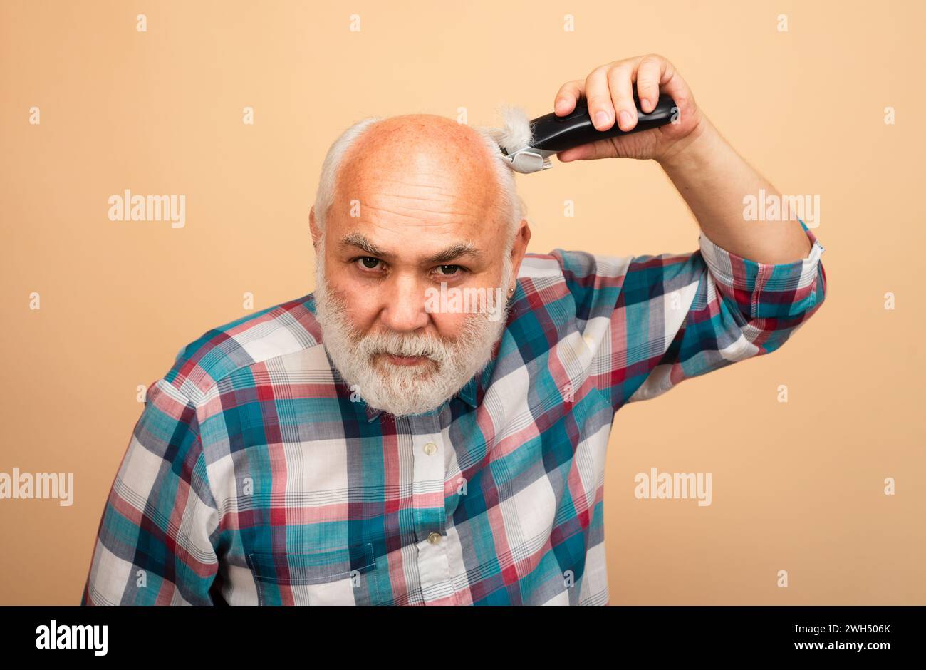 Bearded man cutting his own hair with a clipper. Middle aged bald man ...