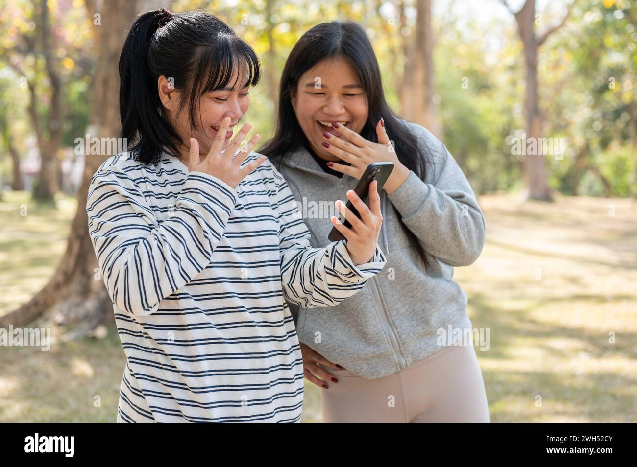 Two young cheerful Asian female best friends are laughing, watching ...