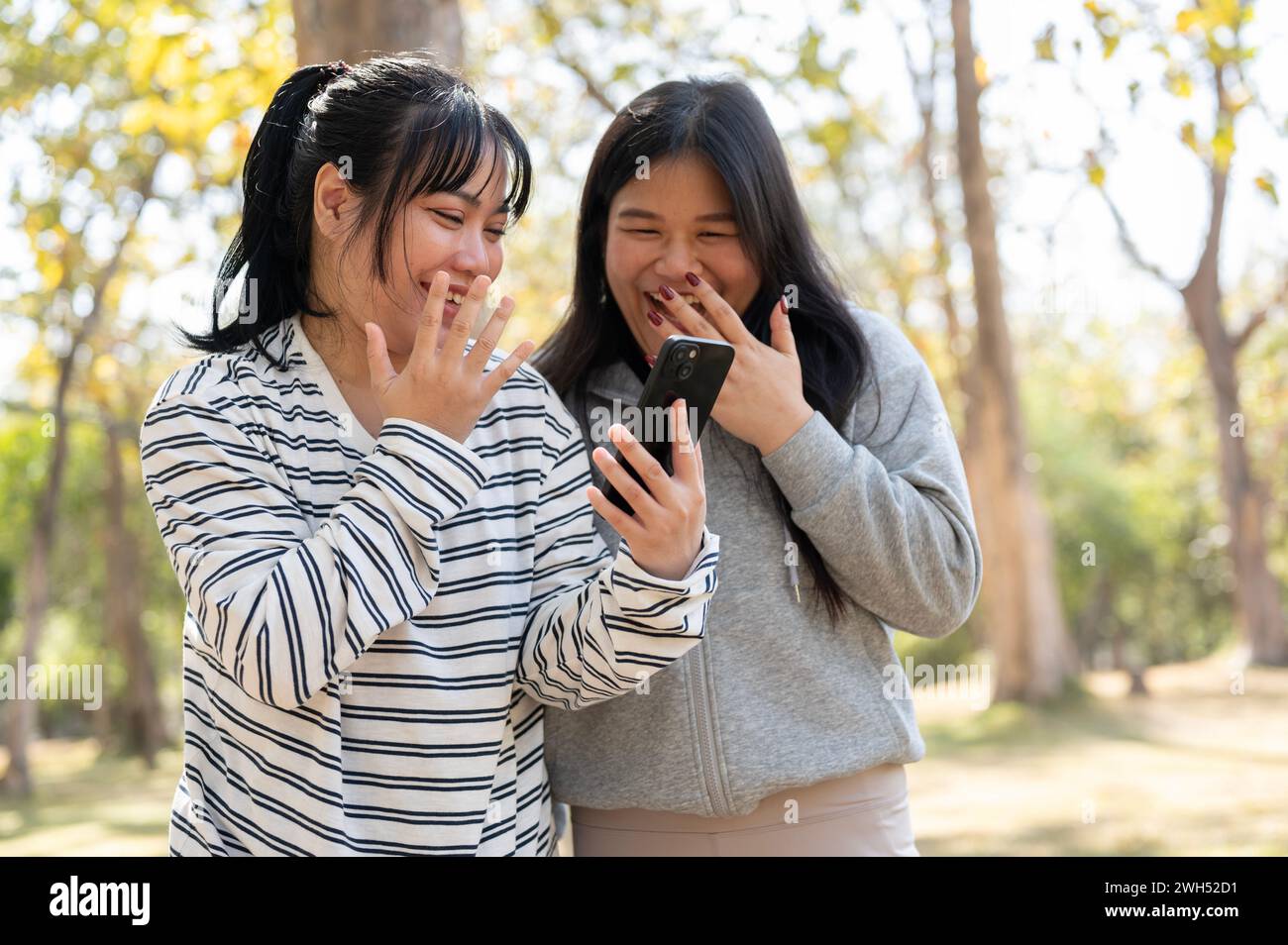 Two young cheerful Asian female best friends are laughing, watching ...