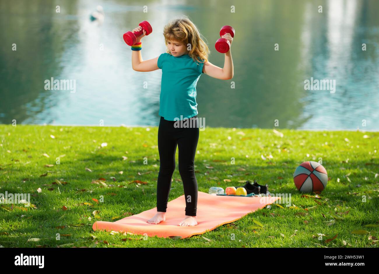 Funny child lifting the dumbbells in backyard outside. Kids in training ...