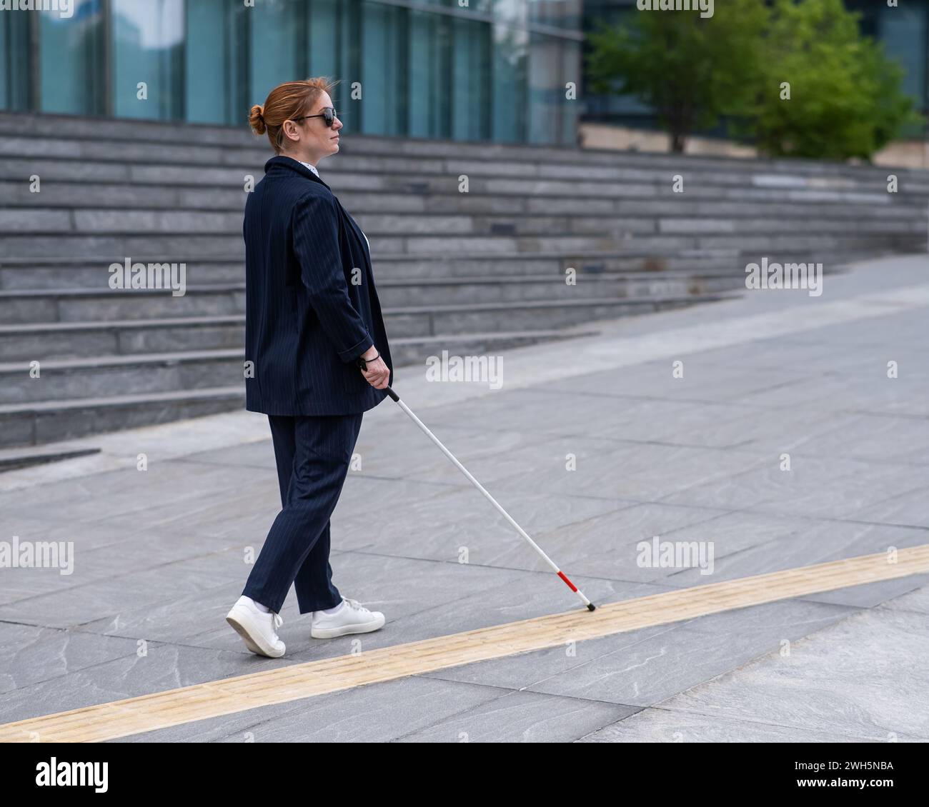 Blind businesswoman walking along tactile tiles with a cane Stock Photo ...
