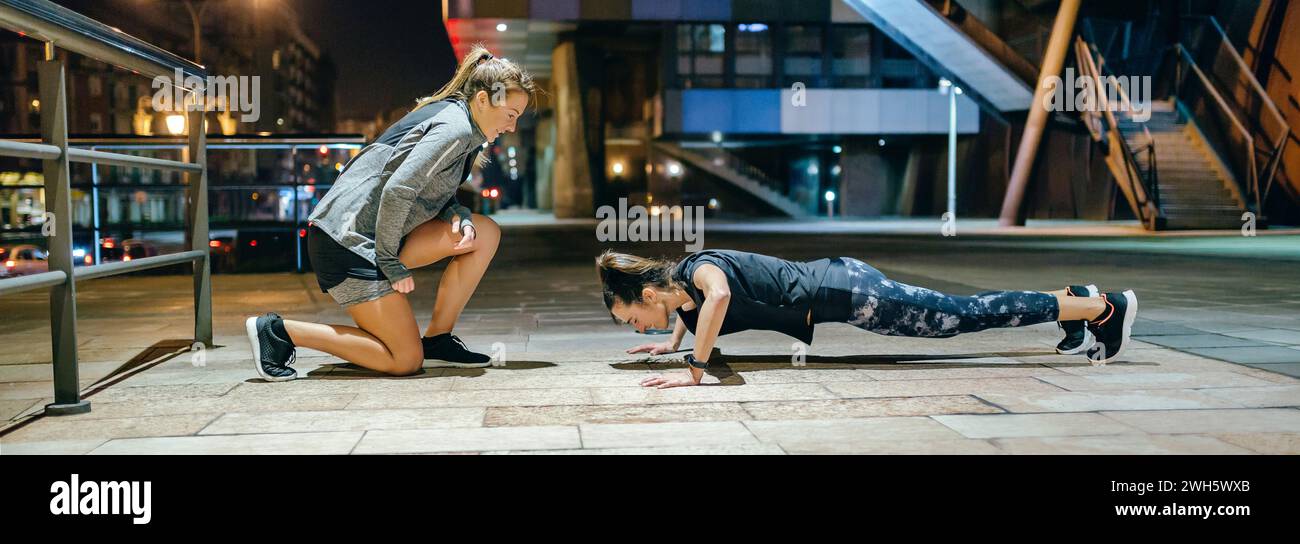 Woman doing push ups by supervision of personal trainer on the city at ...