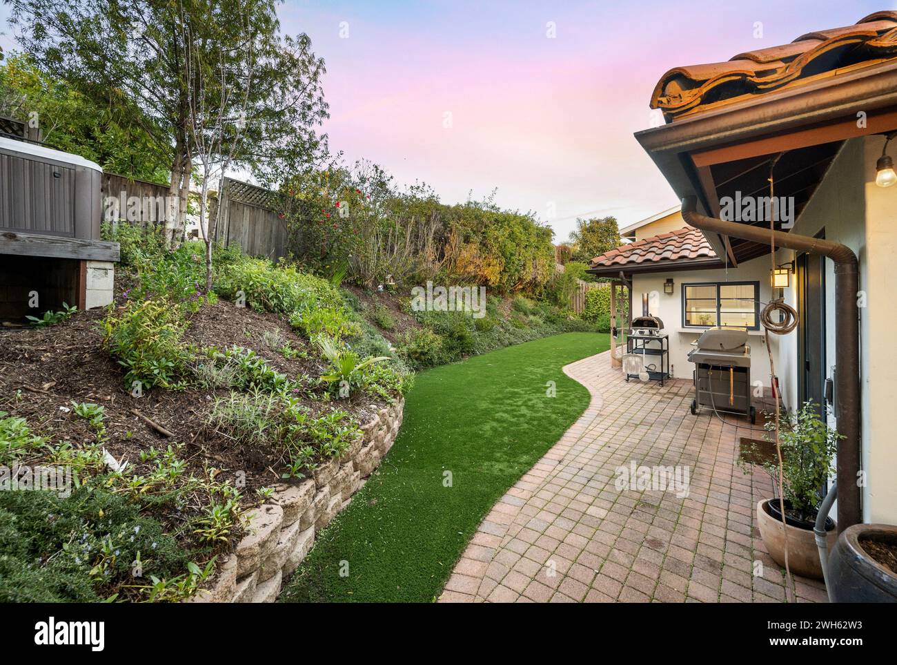 A backyard featuring a charming patio with a BBQ grill and verdant lawn ...
