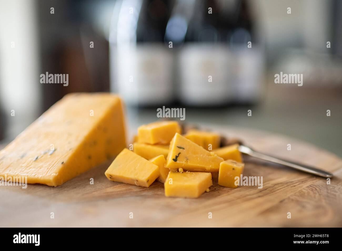 A close-up of cheddar cheese cut on an olive wooden board with a wine ...