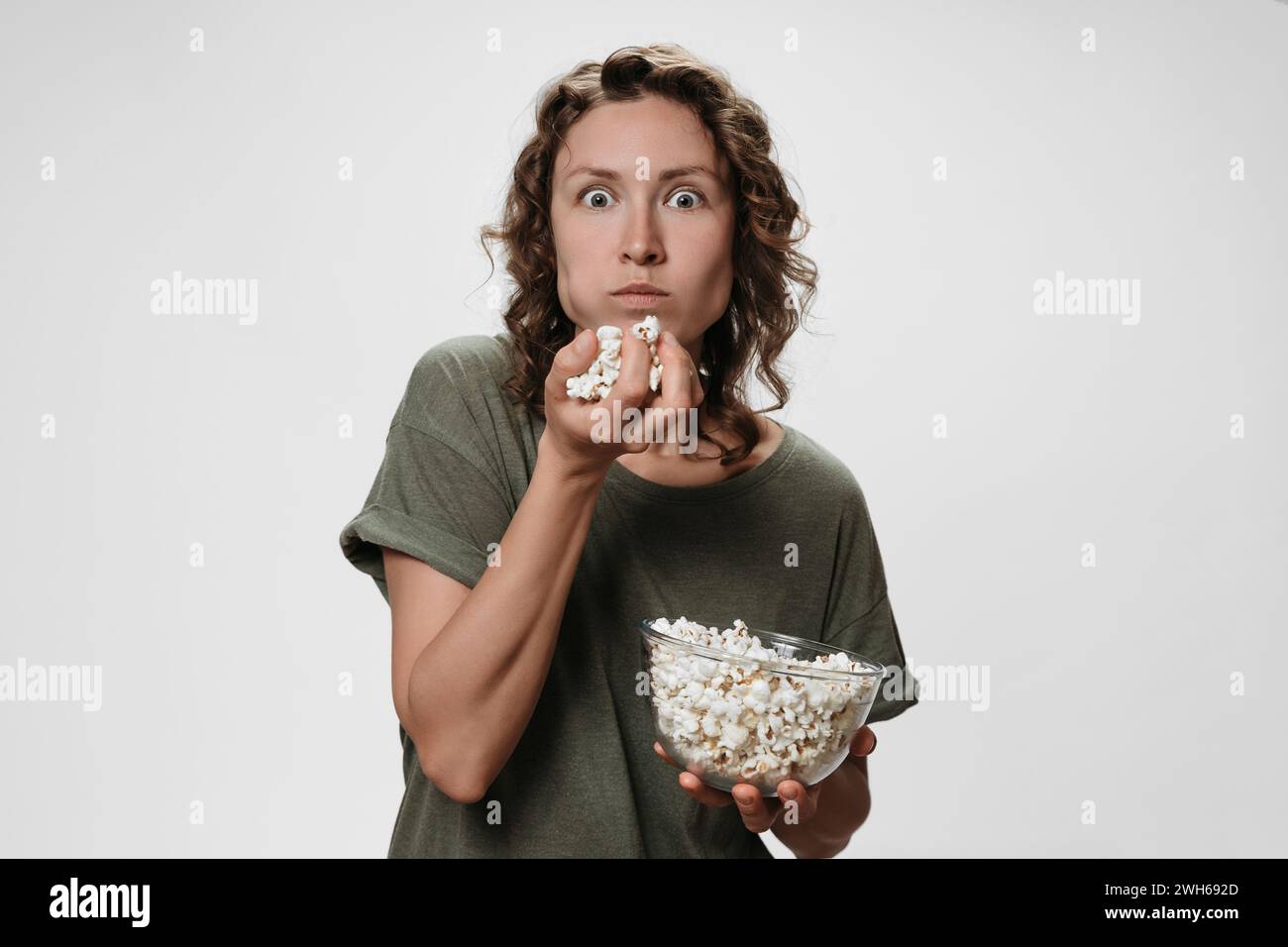 Young woman with curly hair eating popcorn, watching a movie or TV ...