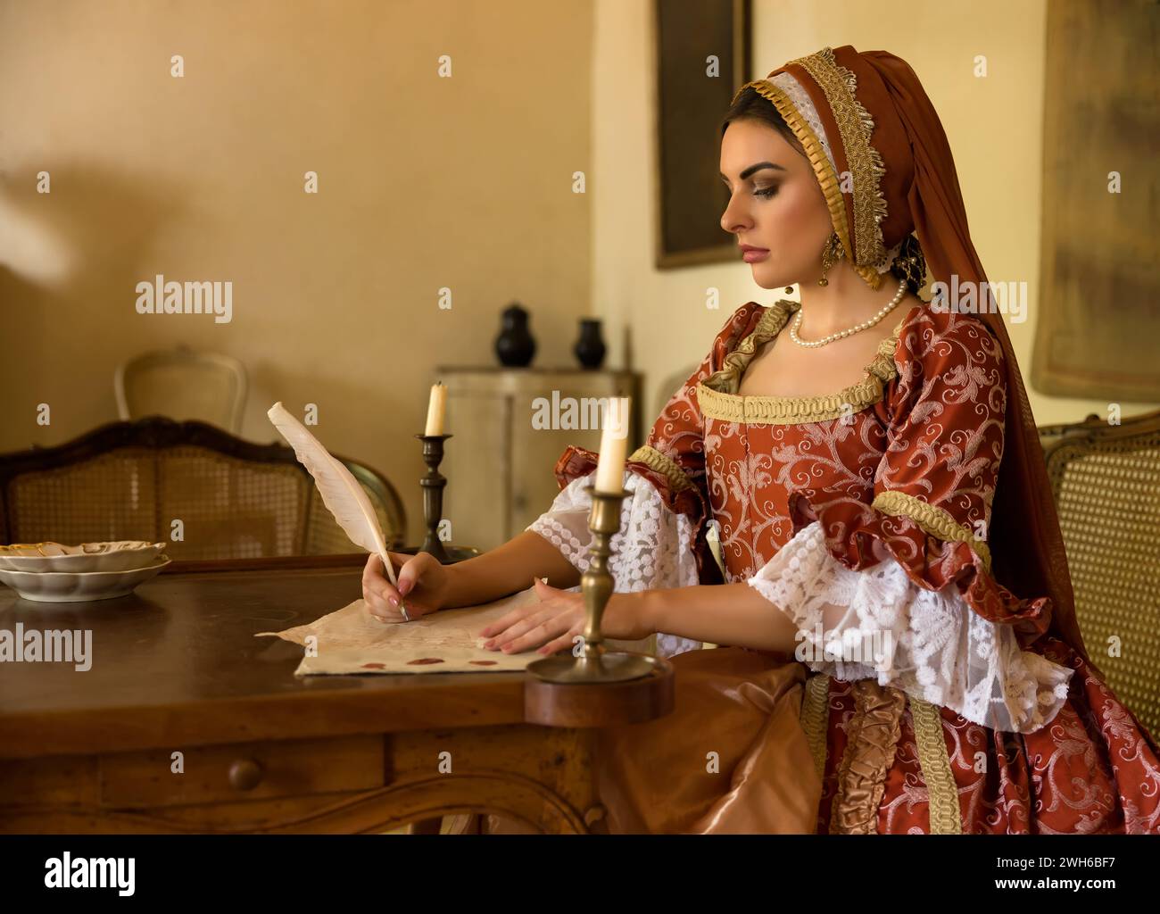 Woman wearing renaissance gown and French hood writing a letter at her ...