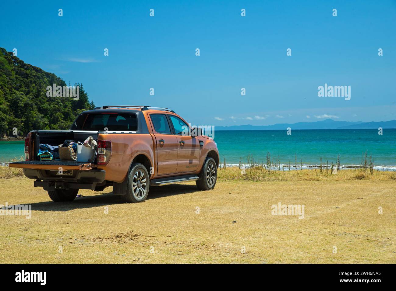 An orange Ford pick up truck parked facing out to sea at Cooks Beach ...