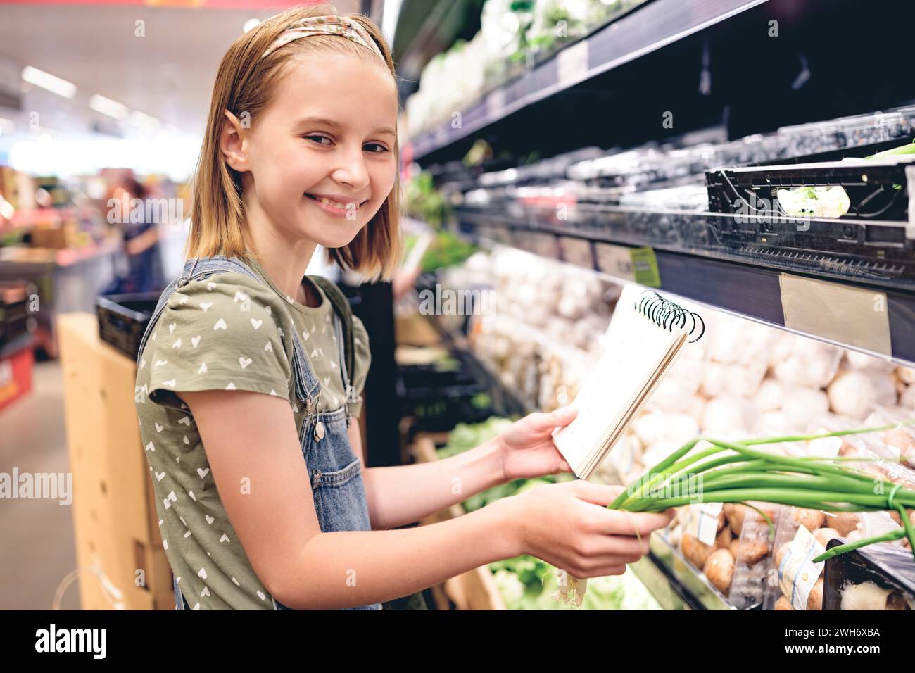 Pretty girl child buying green onion with shopping list in supermarket ...
