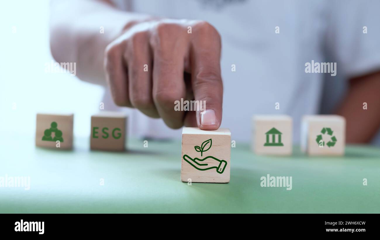 Man's hand touches a wooden cube with environmental and social ...