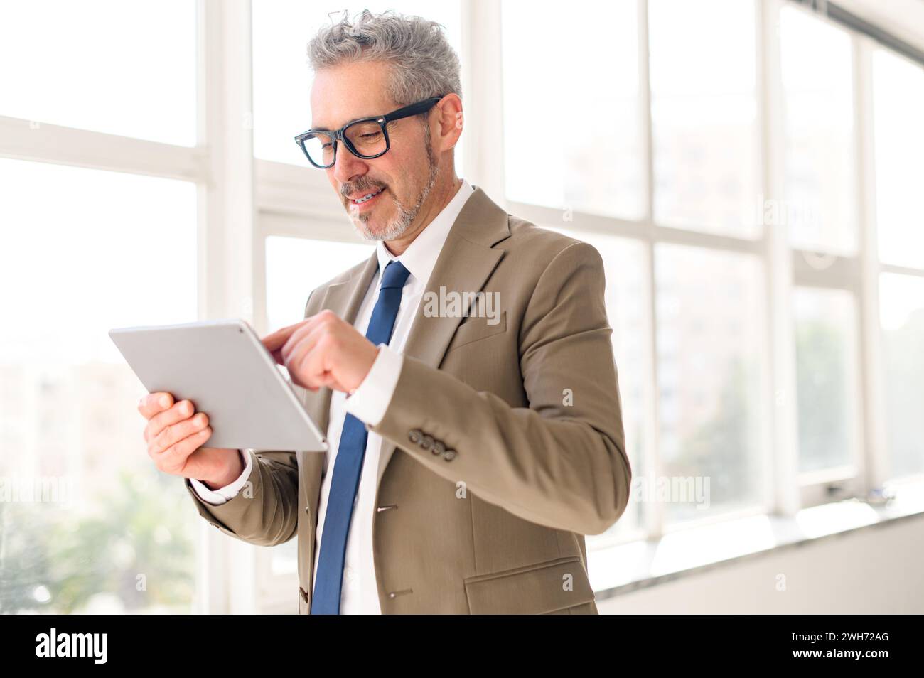The seasoned businessman is interacting with digital tablet in his ...