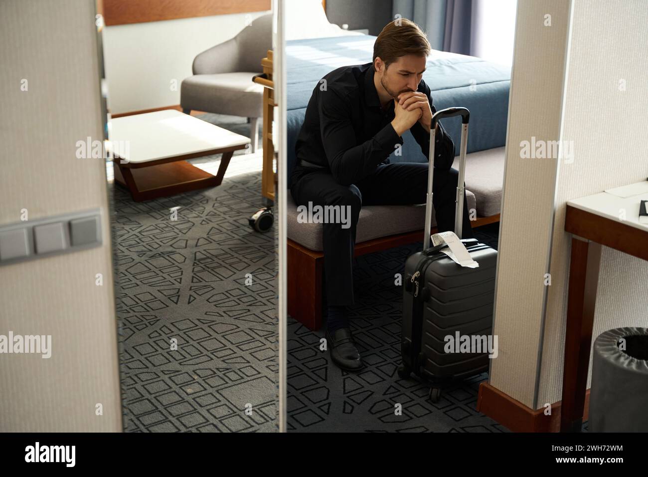 Sad guy in travel clothes sits on a bed in a hotel room Stock Photo - Alamy
