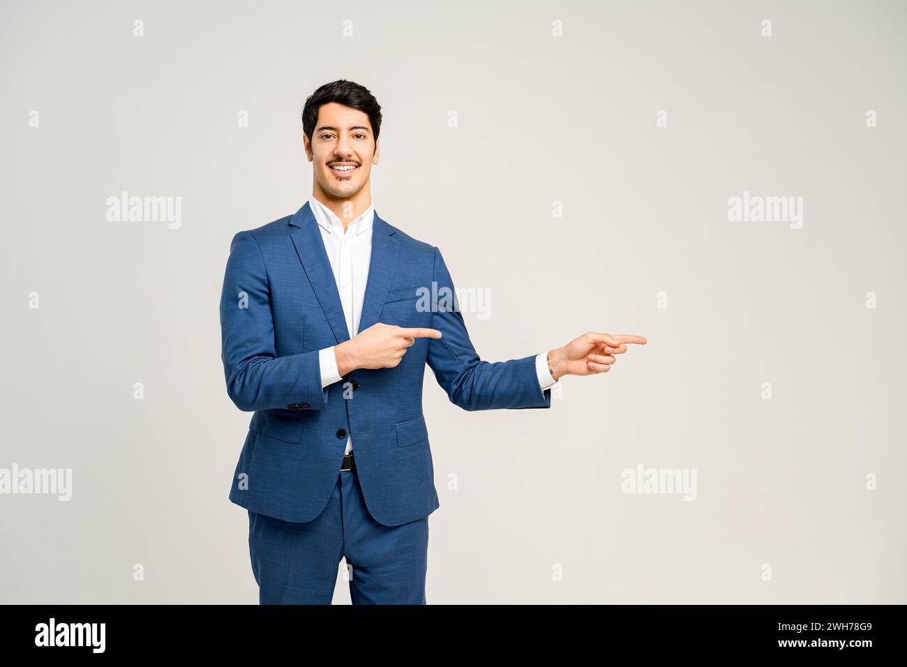 A charming businessman points to the side with a confident smile ...