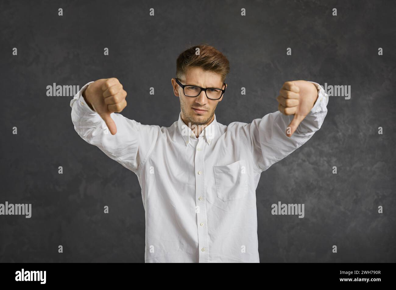 Disappointed young man giving a thumbs down standing isolated on a grey ...