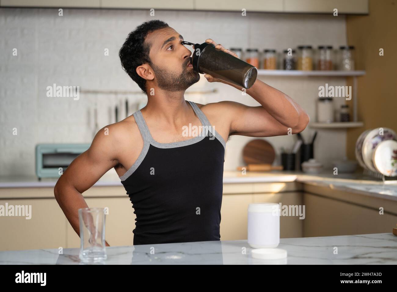 Happy Middle aged fit man drinking protein shake from bottle at kitchen ...