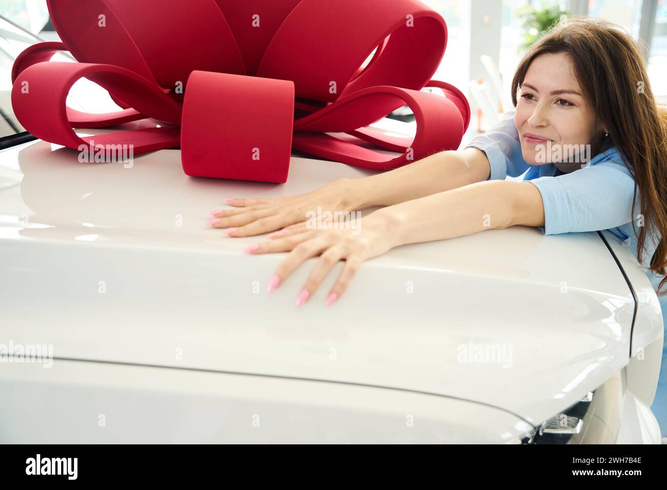 Charming female hugs the hood of car with red bow Stock Photo - Alamy