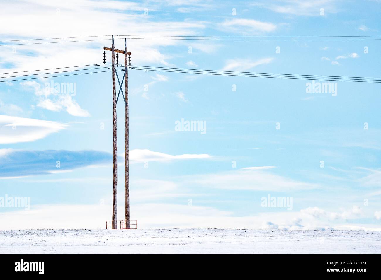 Isolated power pole on a snow covered prairie field with overhead power ...