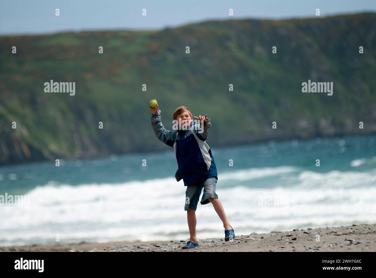 A young boy throws a ball into the distance while playing on a beach ...