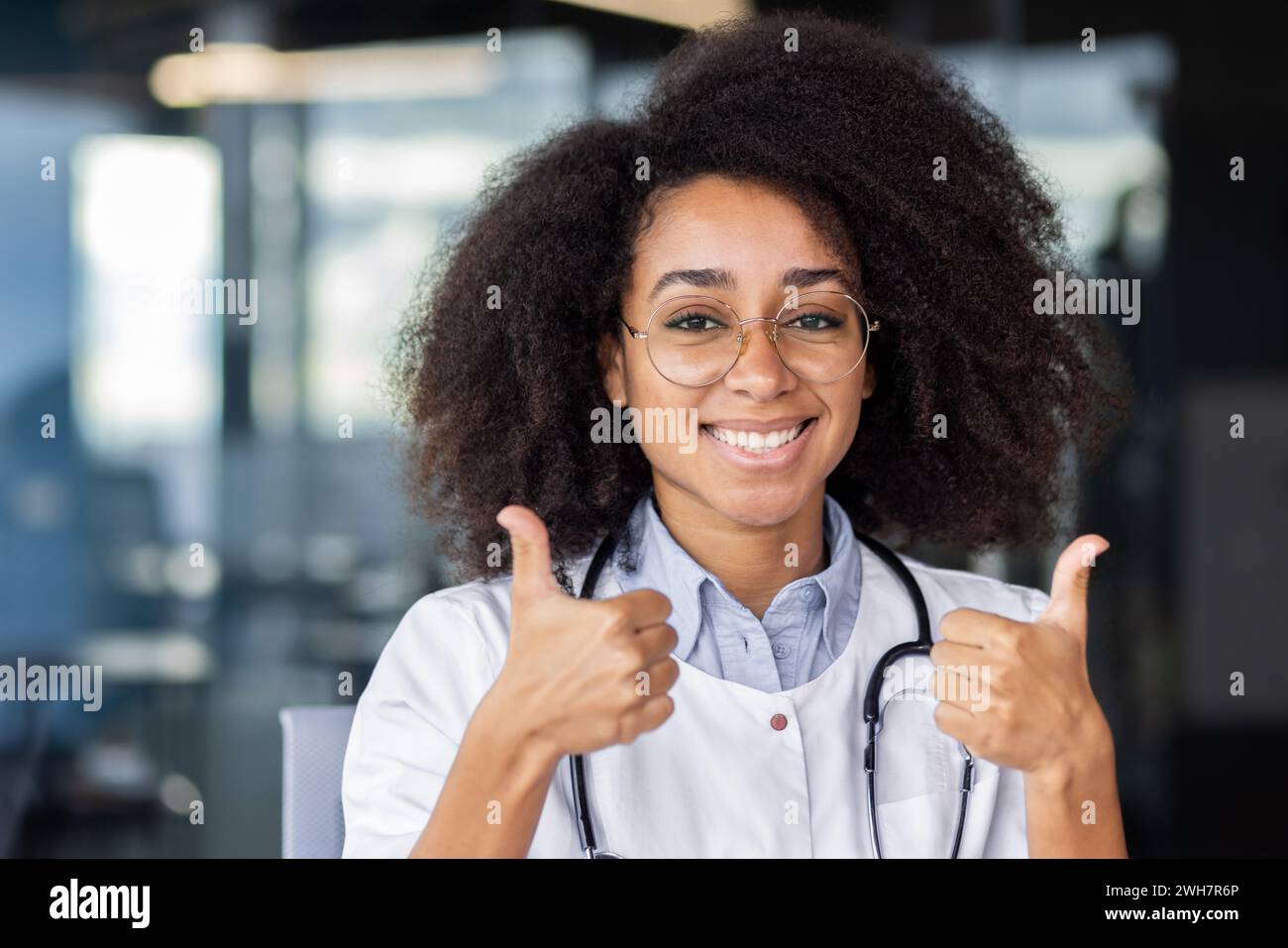 A female doctor with glasses and a smile gives a thumbs up, spreading ...