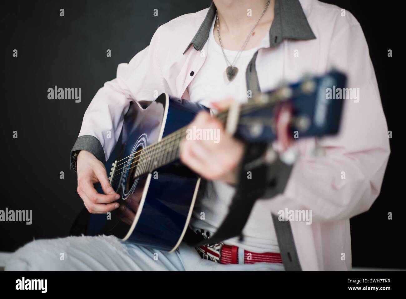 A young slim attractive man in white shirt playing blue guitar on black ...