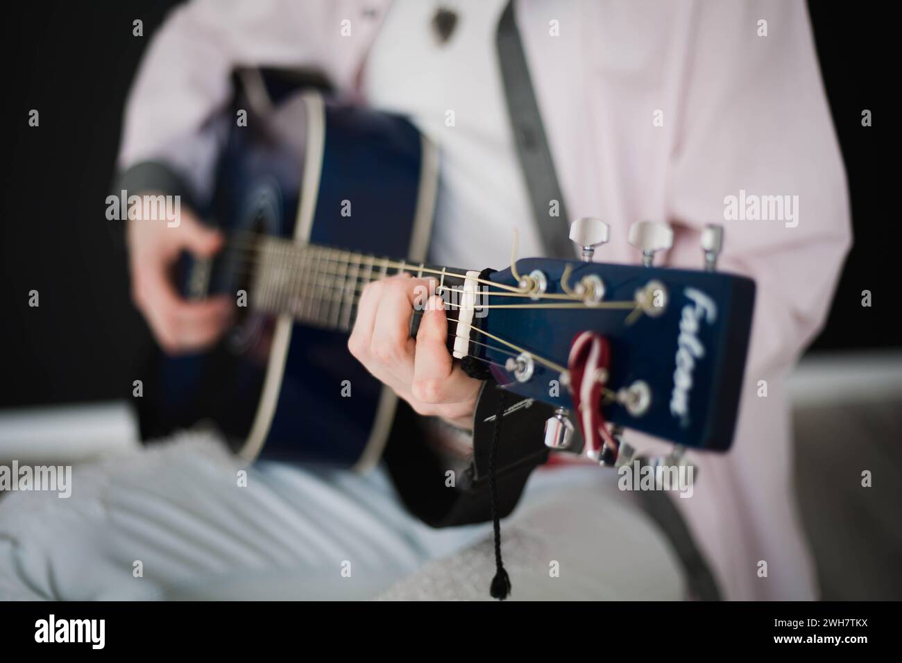 A young slim attractive man in white shirt playing blue guitar on black ...