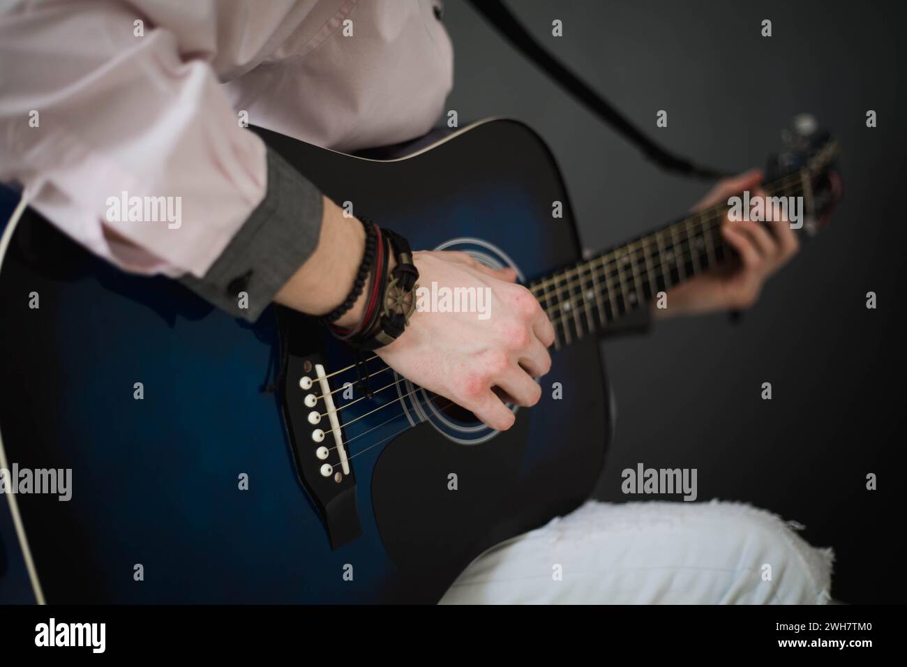 A young slim attractive man in white shirt playing blue guitar on black ...