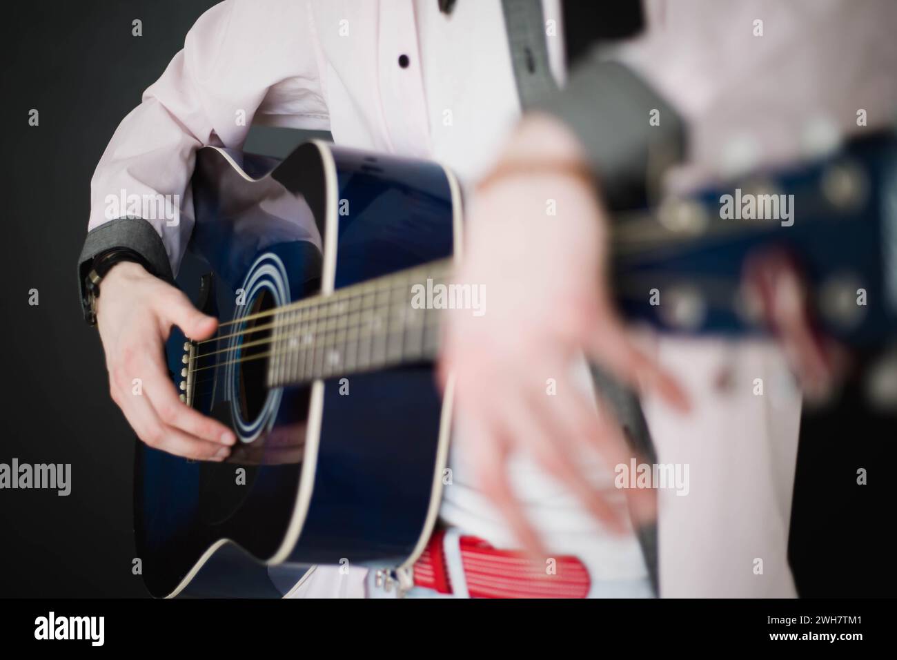 A young slim attractive man in white shirt playing blue guitar on black ...
