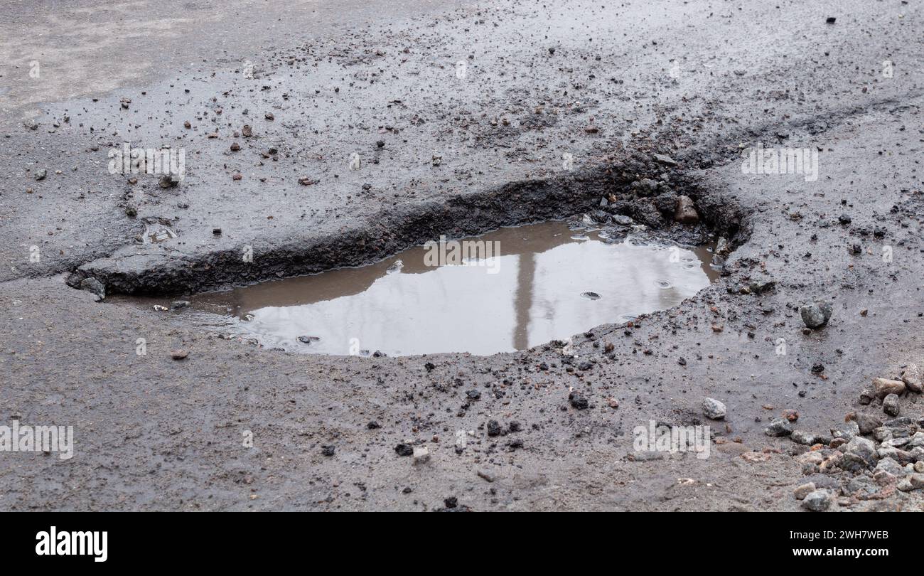 Deep pit on the road with puddle. Damaged asphalt after winter. Road ...