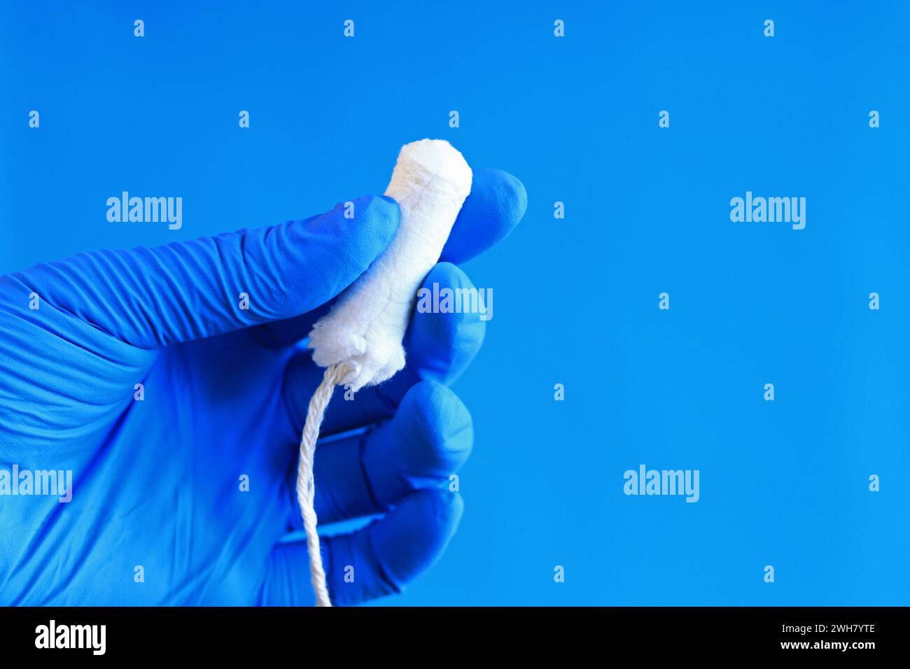 Female hand with a tampon close-up on a blue background. A hand in a ...