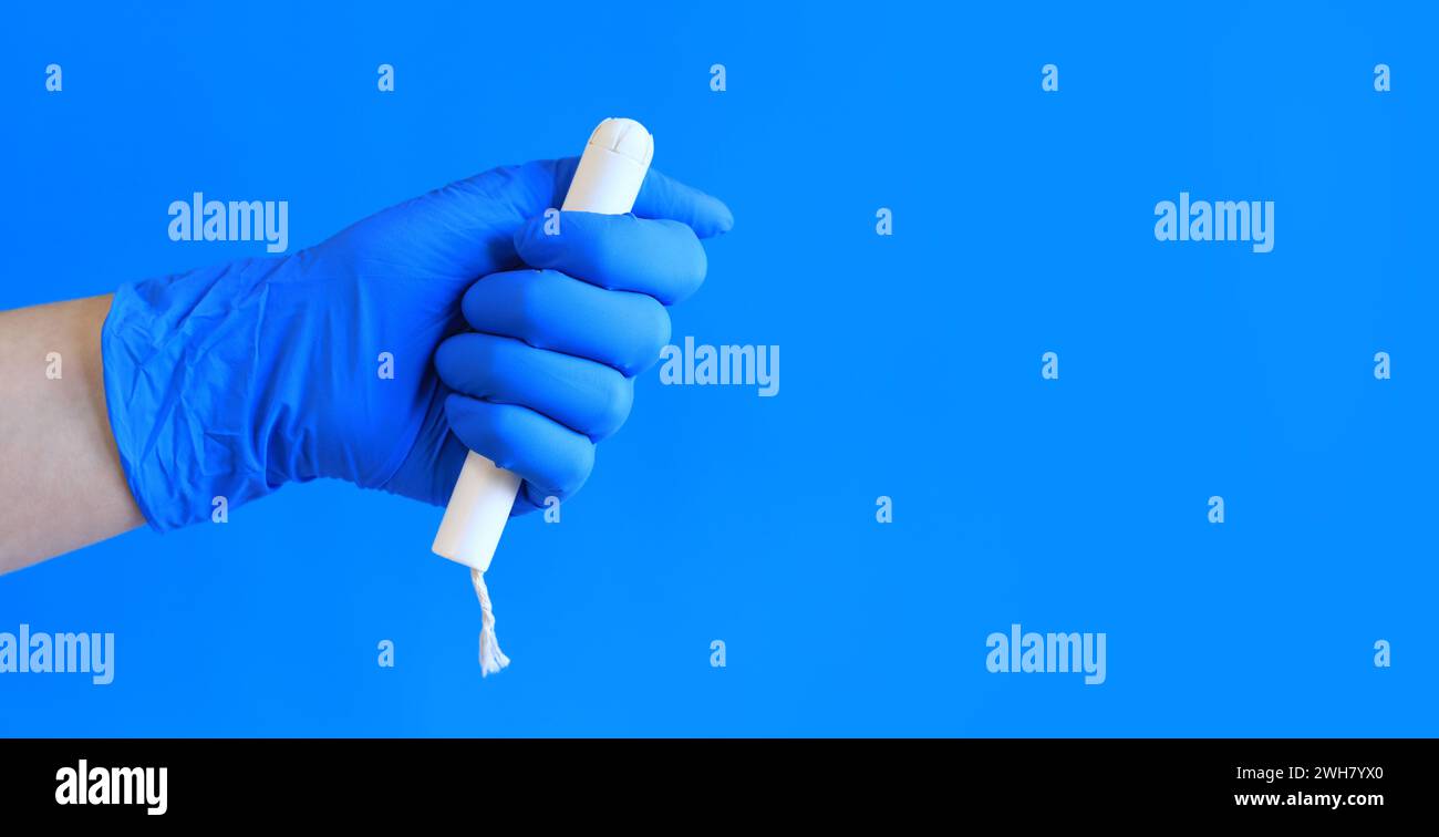 Tampon in a cardboard applicator in a woman's hand, blue background. A ...