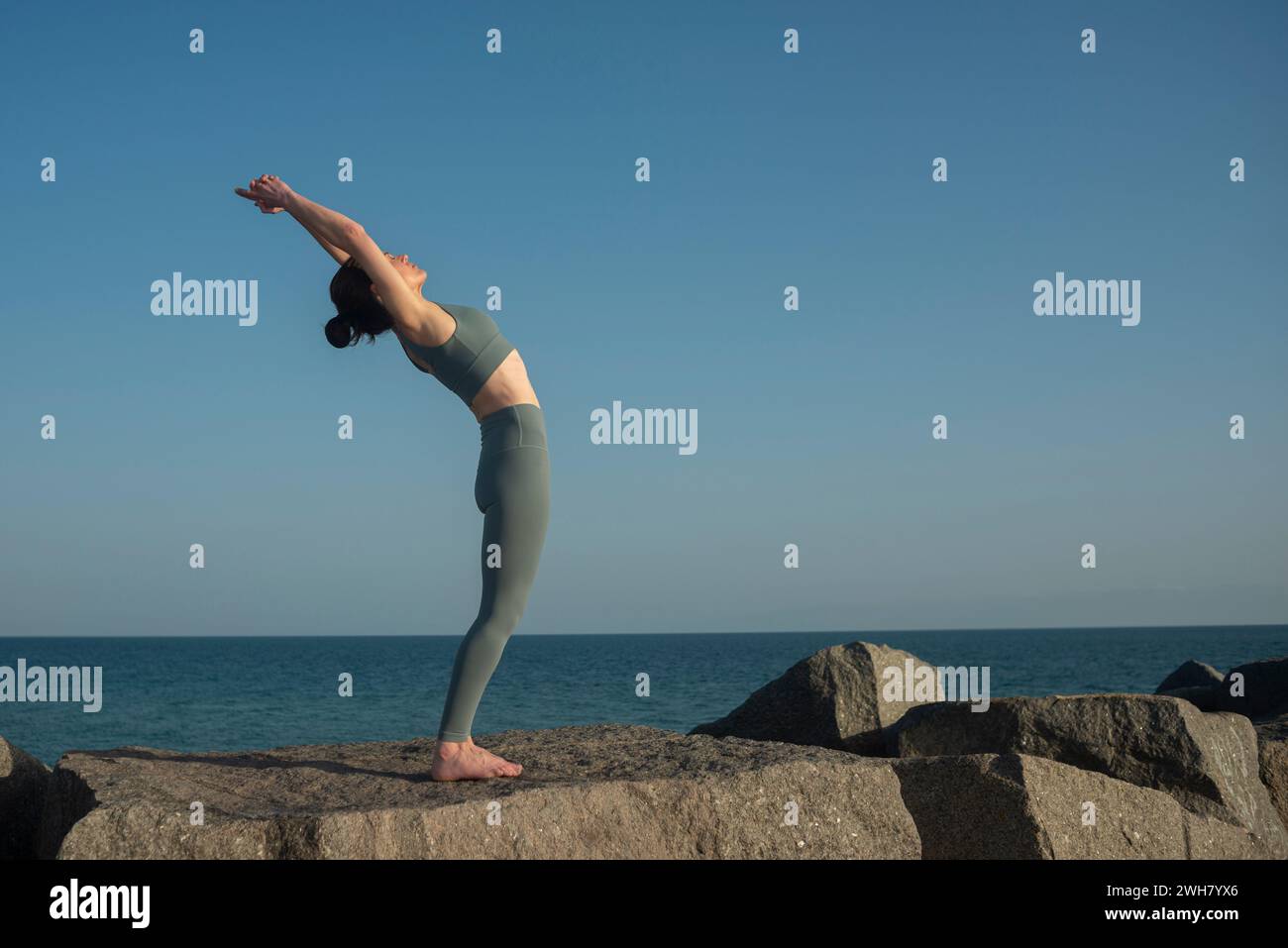 fit woman doing a backbend stretch on the rocks, blue sky background ...