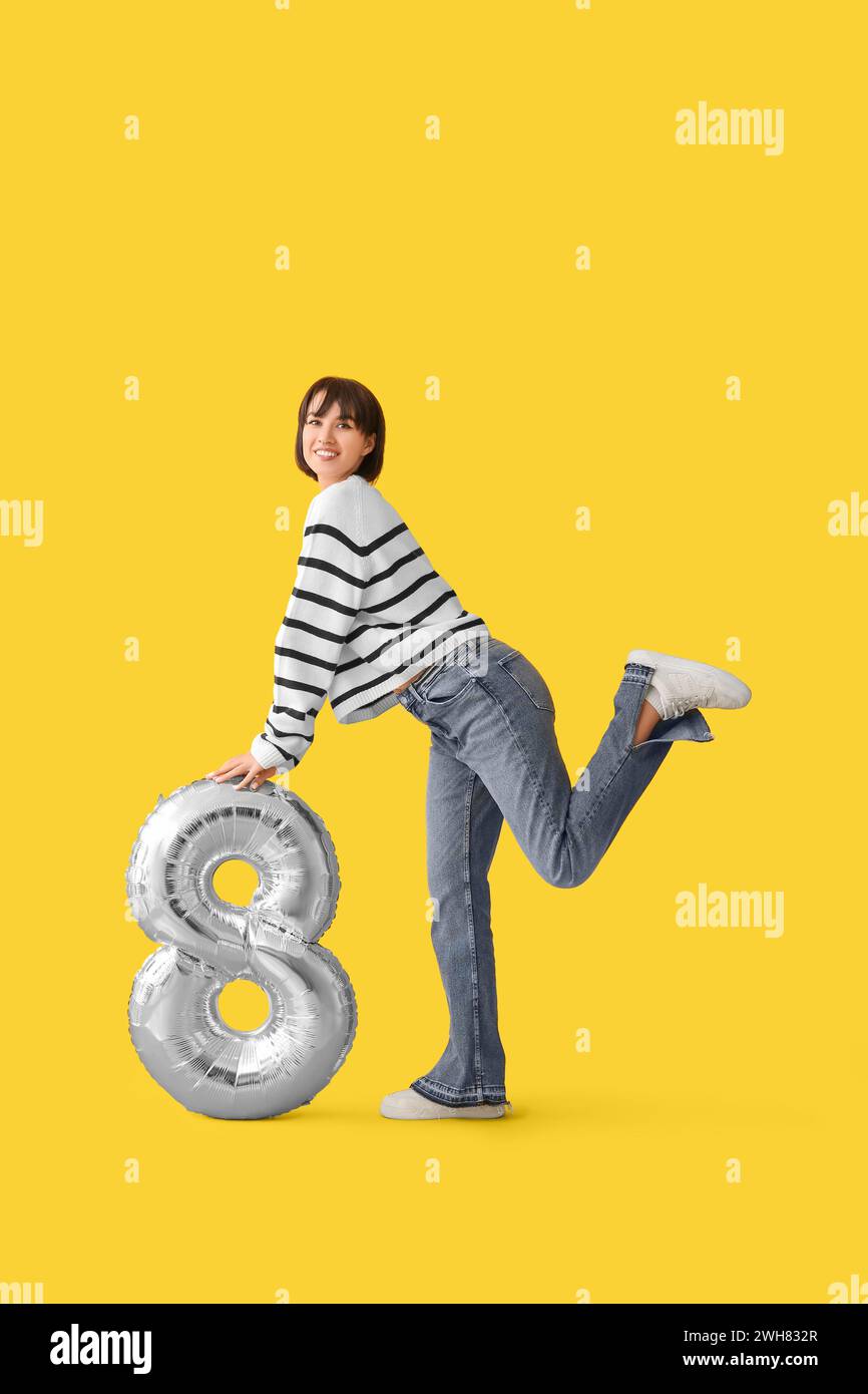 Beautiful young woman with balloon in shape of figure 8 on yellow ...
