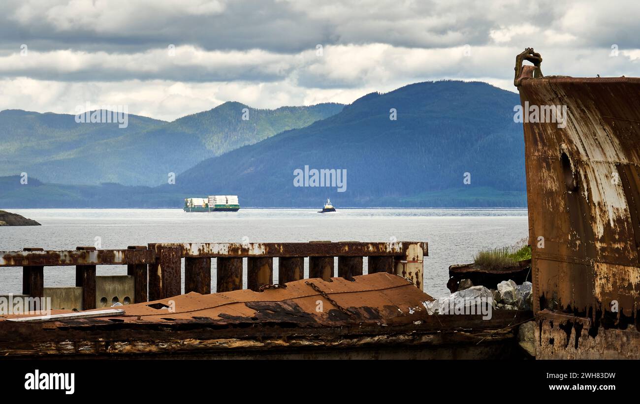 Old rusty ship hulls act as a breakwater. Tug and barge coming down the ...