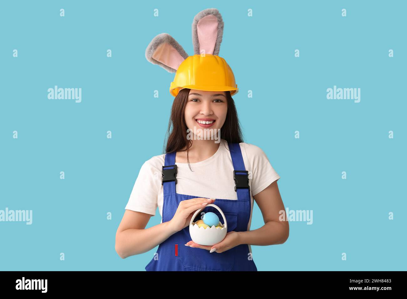 Female Asian worker in bunny ears with Easter eggs on blue background ...
