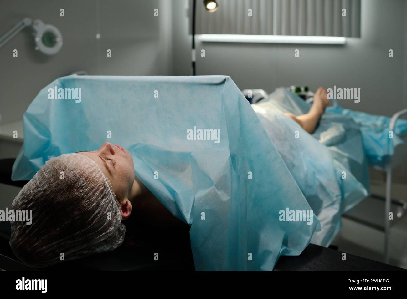 Young sleeping female patient under blue cover lying in operating room ...