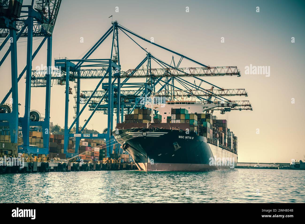 A large container ship is unloaded by large cargo cranes in the ...