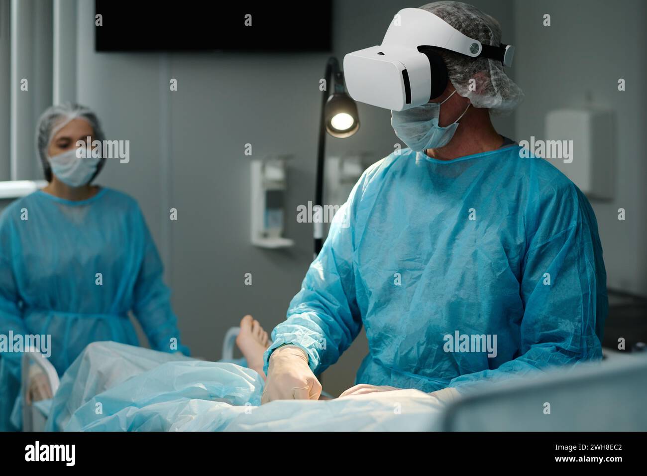 Mature surgeon in VR headset, scrubs, protective mask and gloves using ...