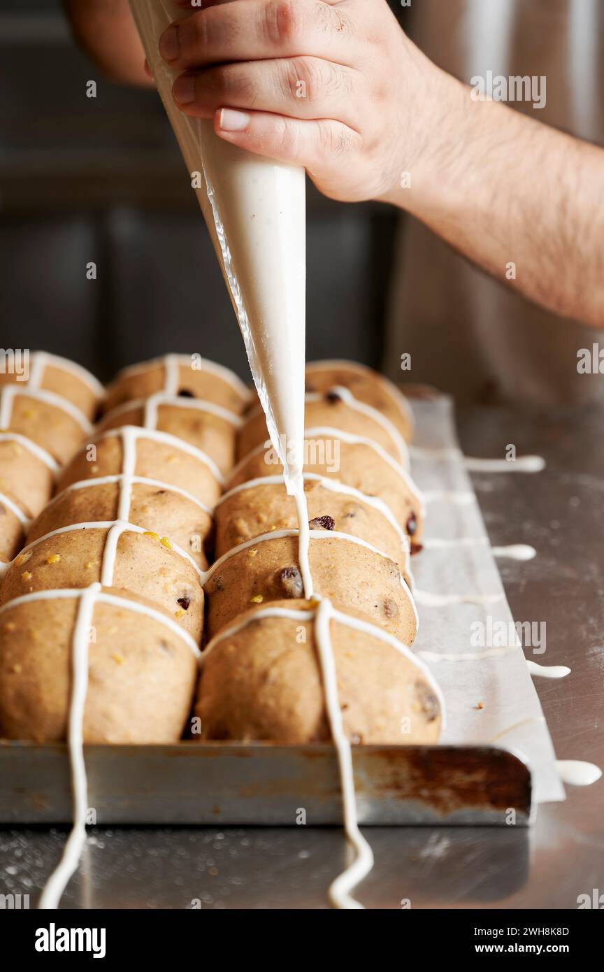 Baker piping 'cross' onto uncooked fruit hot cross buns made with yeast ...