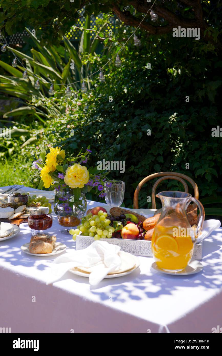 Al fresco summer outdoor dining table laid with fruit, bread tray and ...