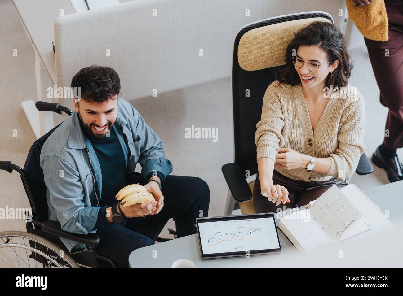 Male employee in wheelchair holding bananas and joking with his ...