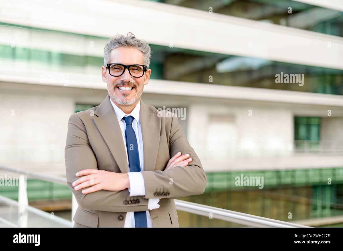 A senior executive stands with crossed arms, exuding a sense of ...