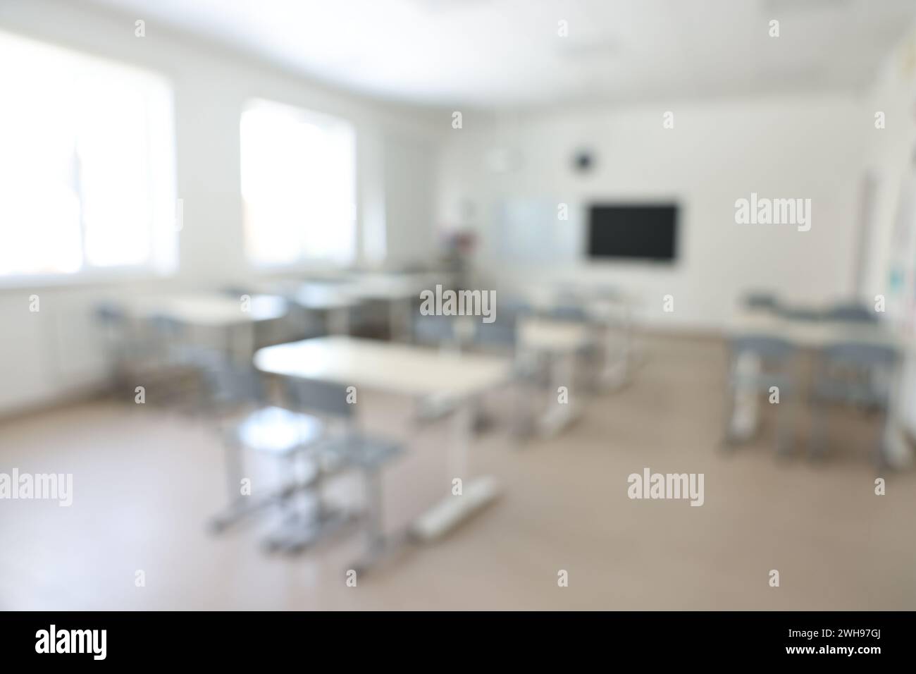 Blurred view of empty school classroom with desks, windows and chairs ...