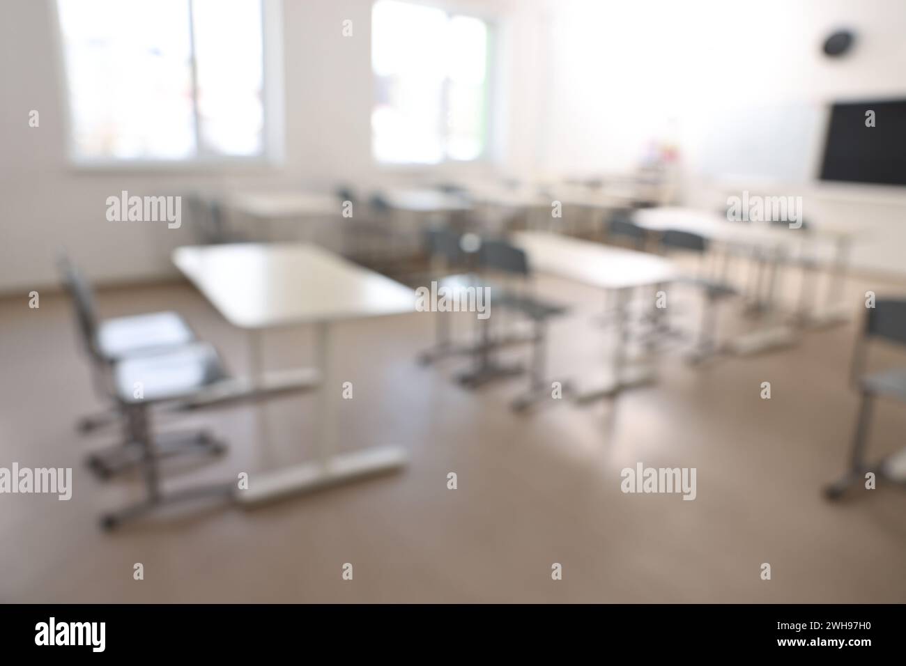 Blurred view of empty school classroom with desks, windows and chairs ...