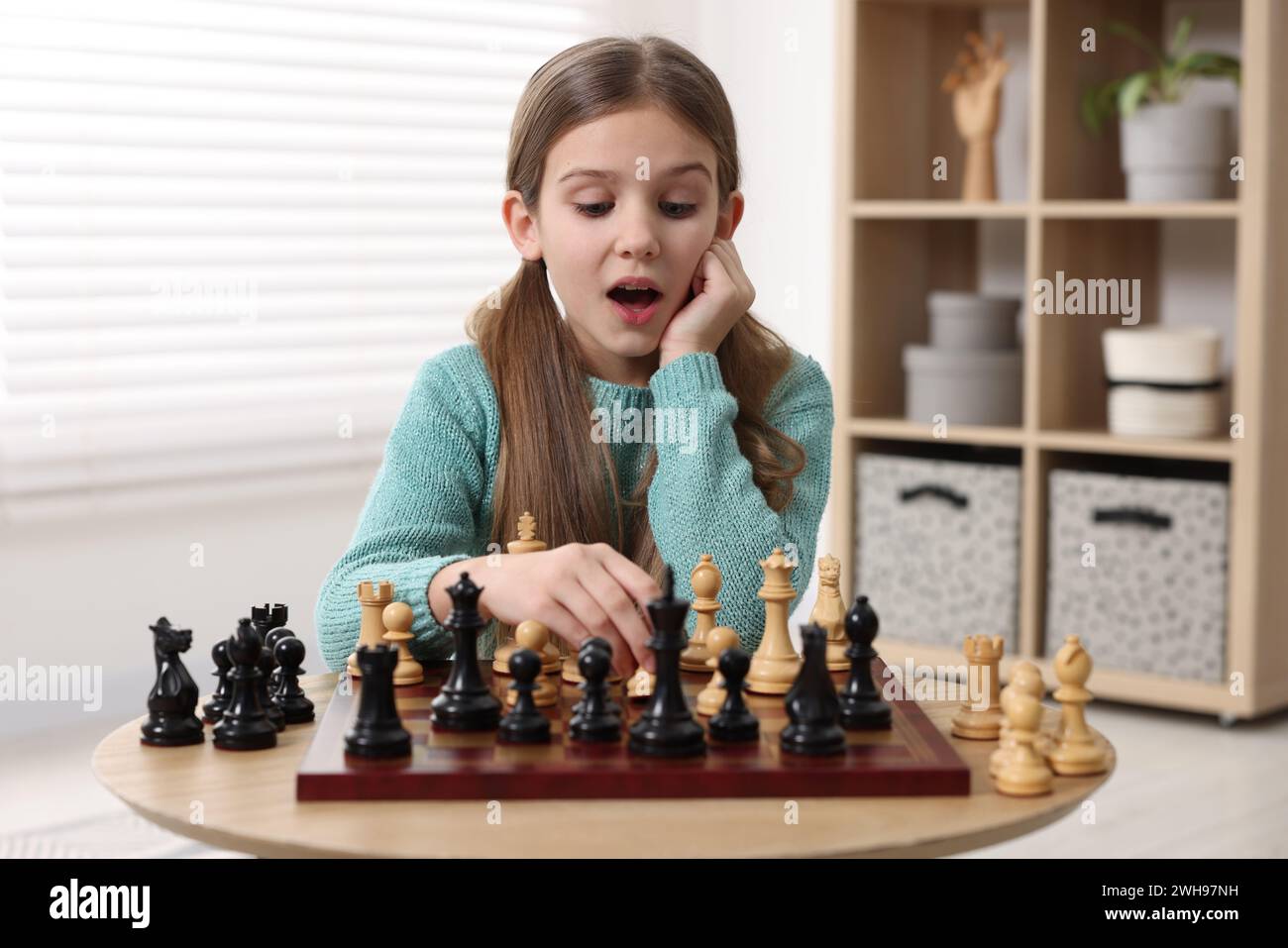 Cute girl playing chess at table in room Stock Photo - Alamy