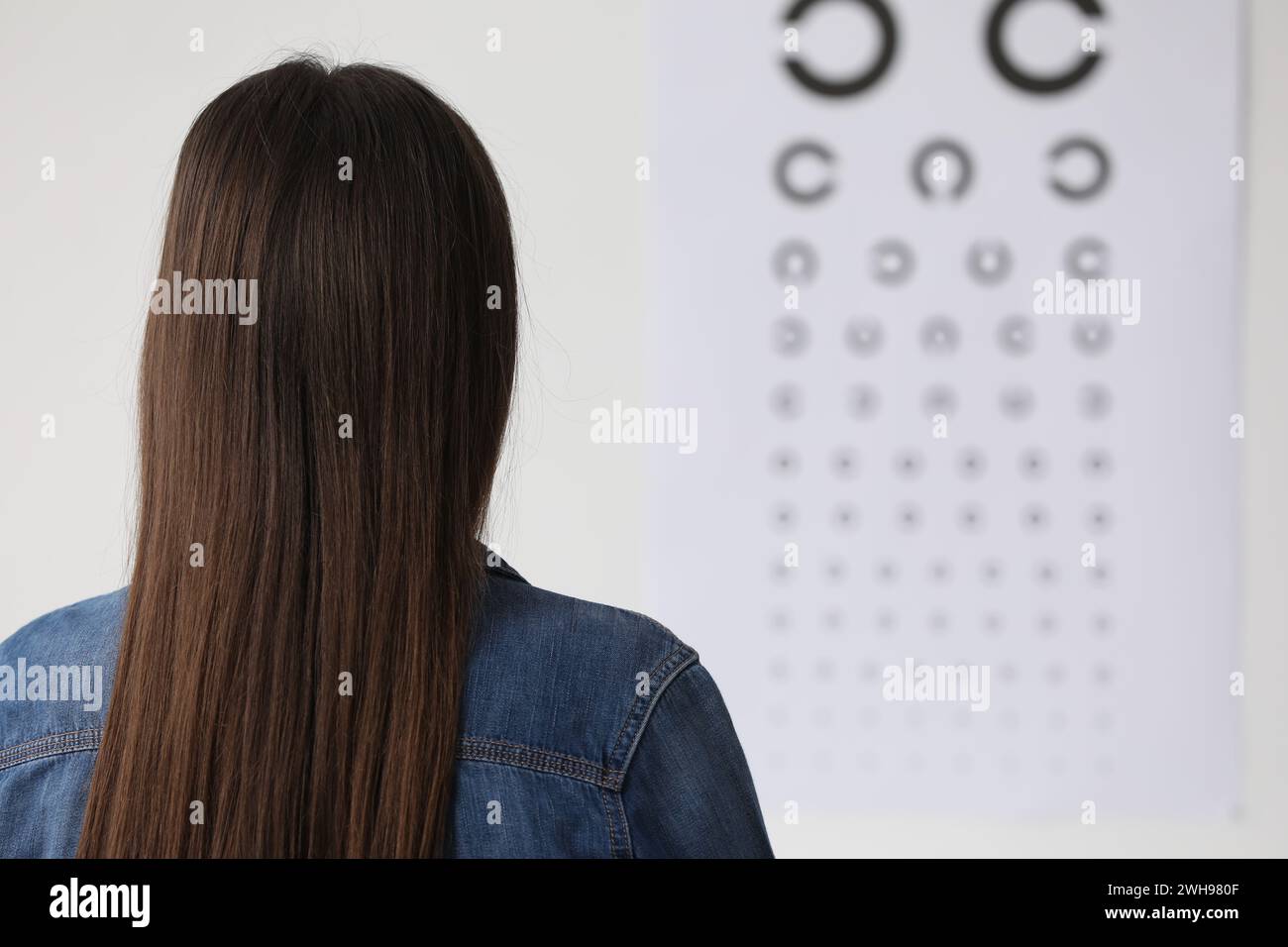Eyesight examination. Young woman looking at vision test chart indoors ...