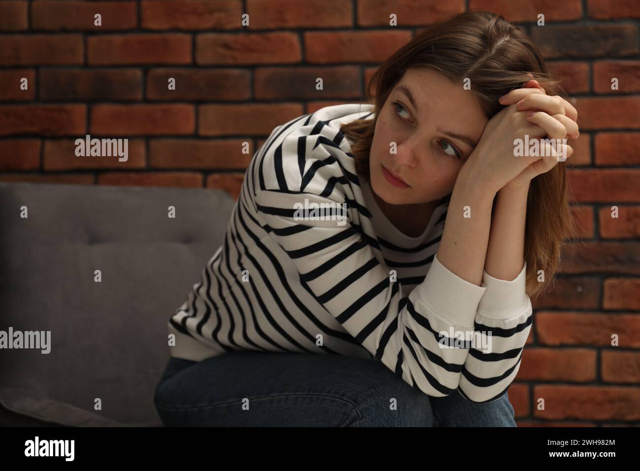 Sad young woman sitting on chair near brick wall Stock Photo - Alamy