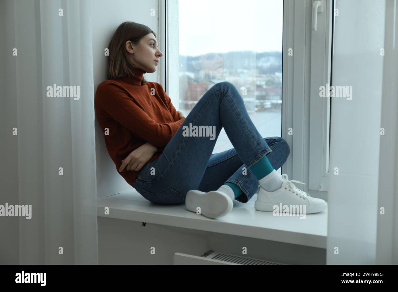 Sad young woman sitting on windowsill near window at home Stock Photo ...