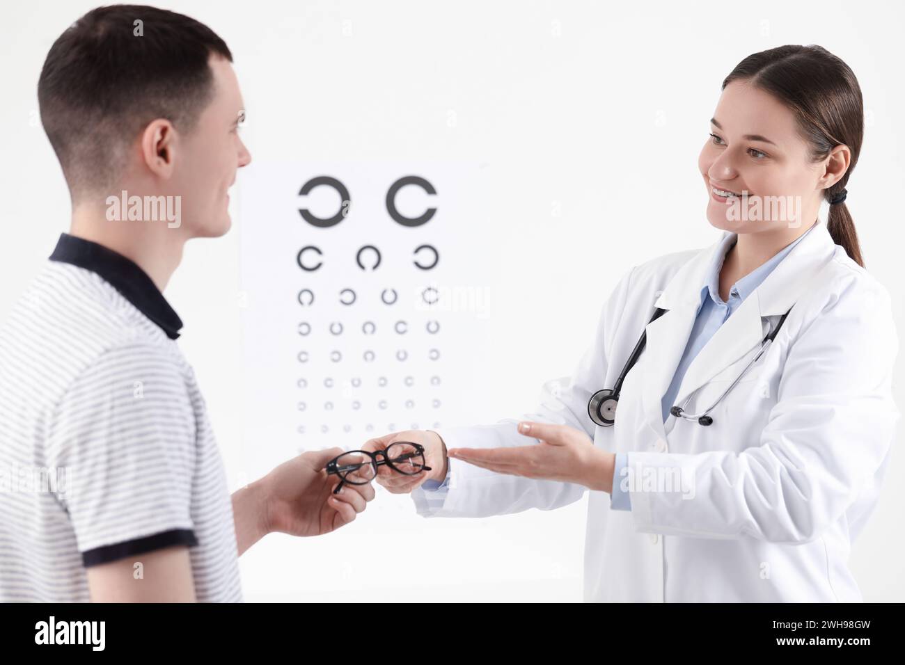 Vision testing. Ophthalmologist giving glasses to young man indoors ...