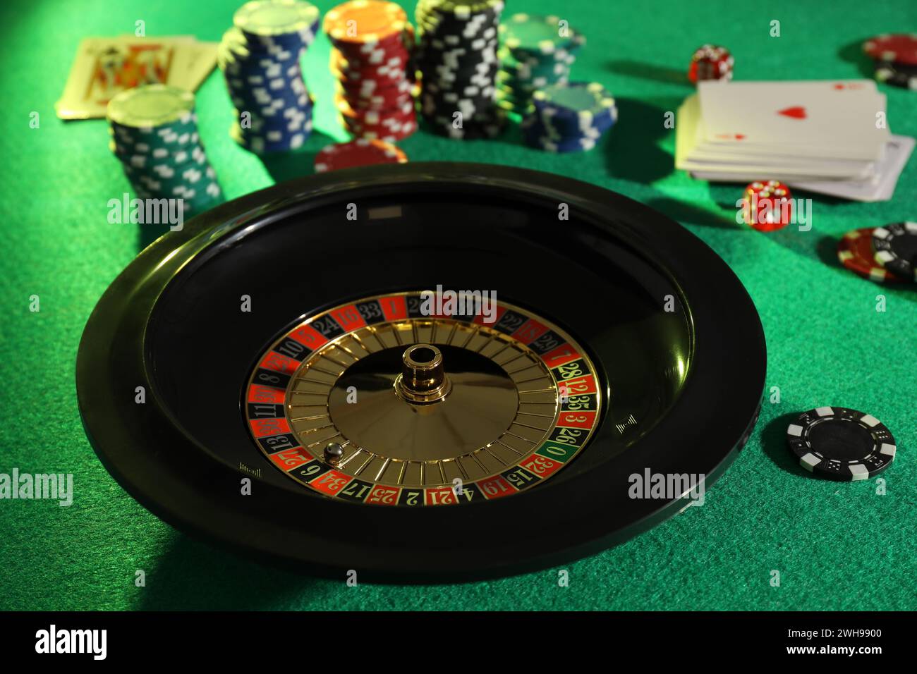 Roulette wheel with ball, playing cards and chips on green table ...