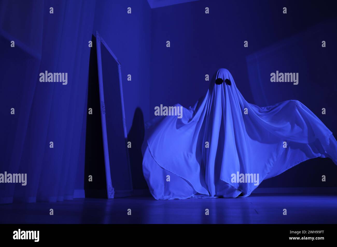 Creepy ghost. Woman covered with sheet in blue light, low angle view ...