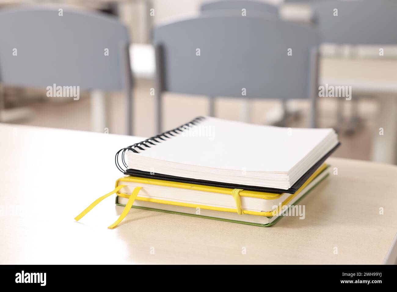 Stack of notebooks on wooden desk in empty classroom Stock Photo - Alamy